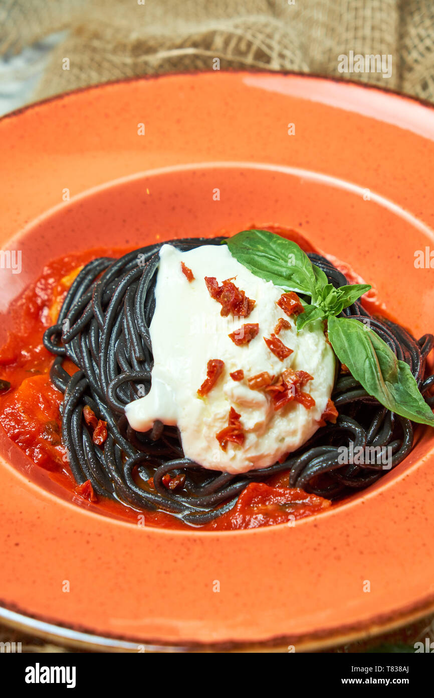 Spaghetti with cuttlefish ink with cream sauce on an orange plate. Gray ...