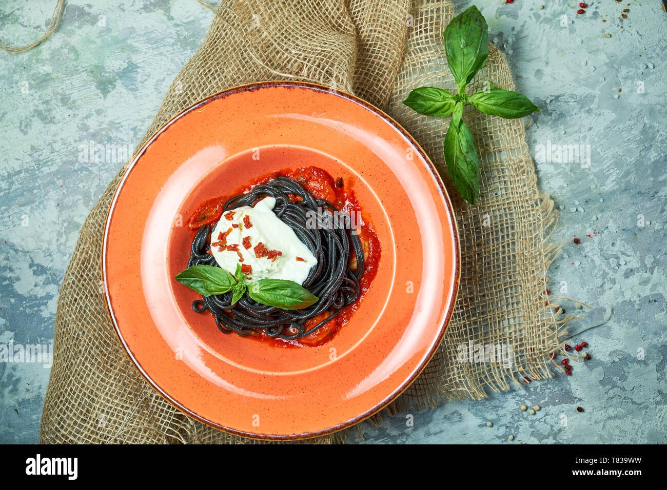 Spaghetti with cuttlefish ink with cream sauce on an orange plate. Gray ...