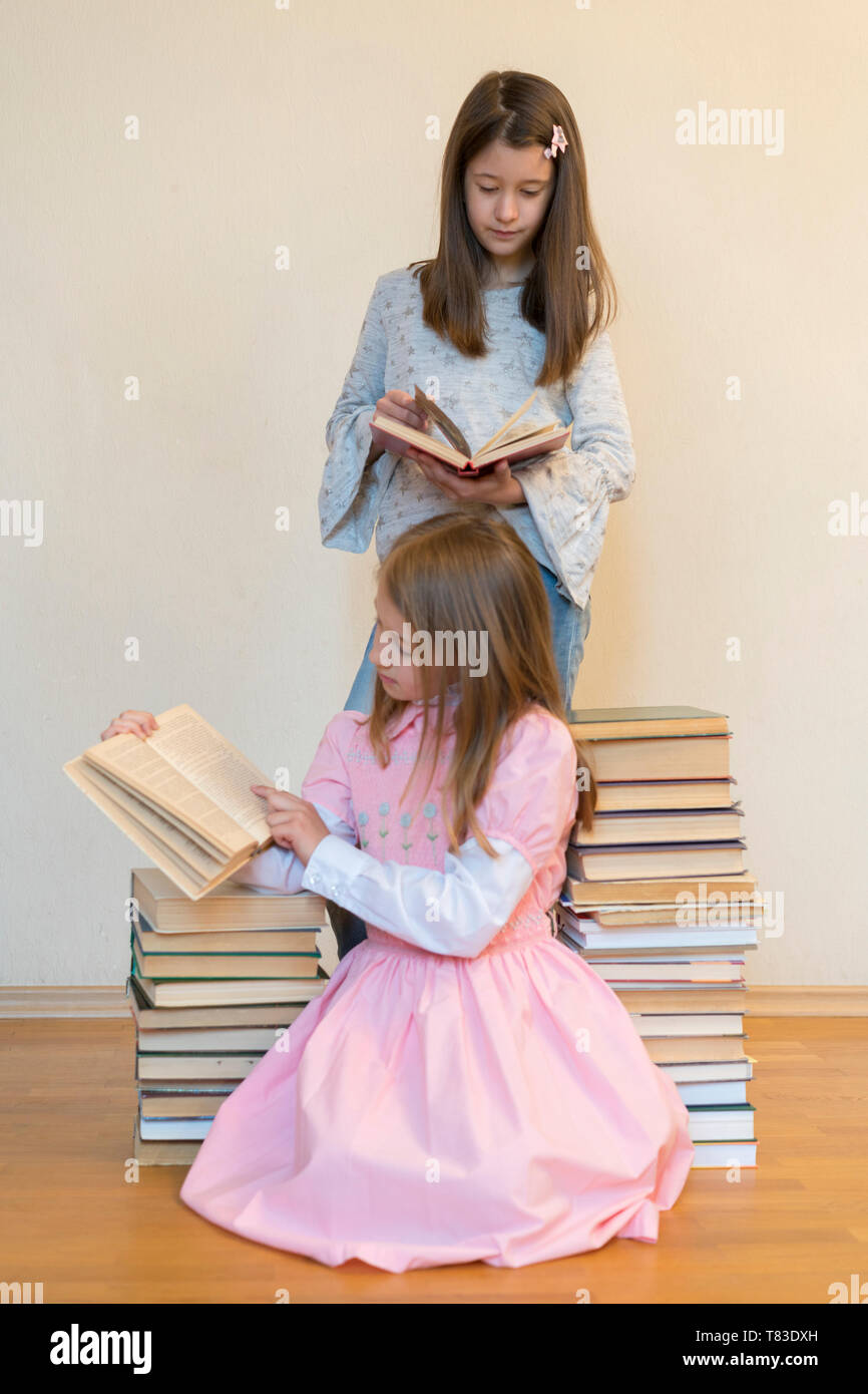 Two sisters with a pile of books on the floor in the room. The concept ...