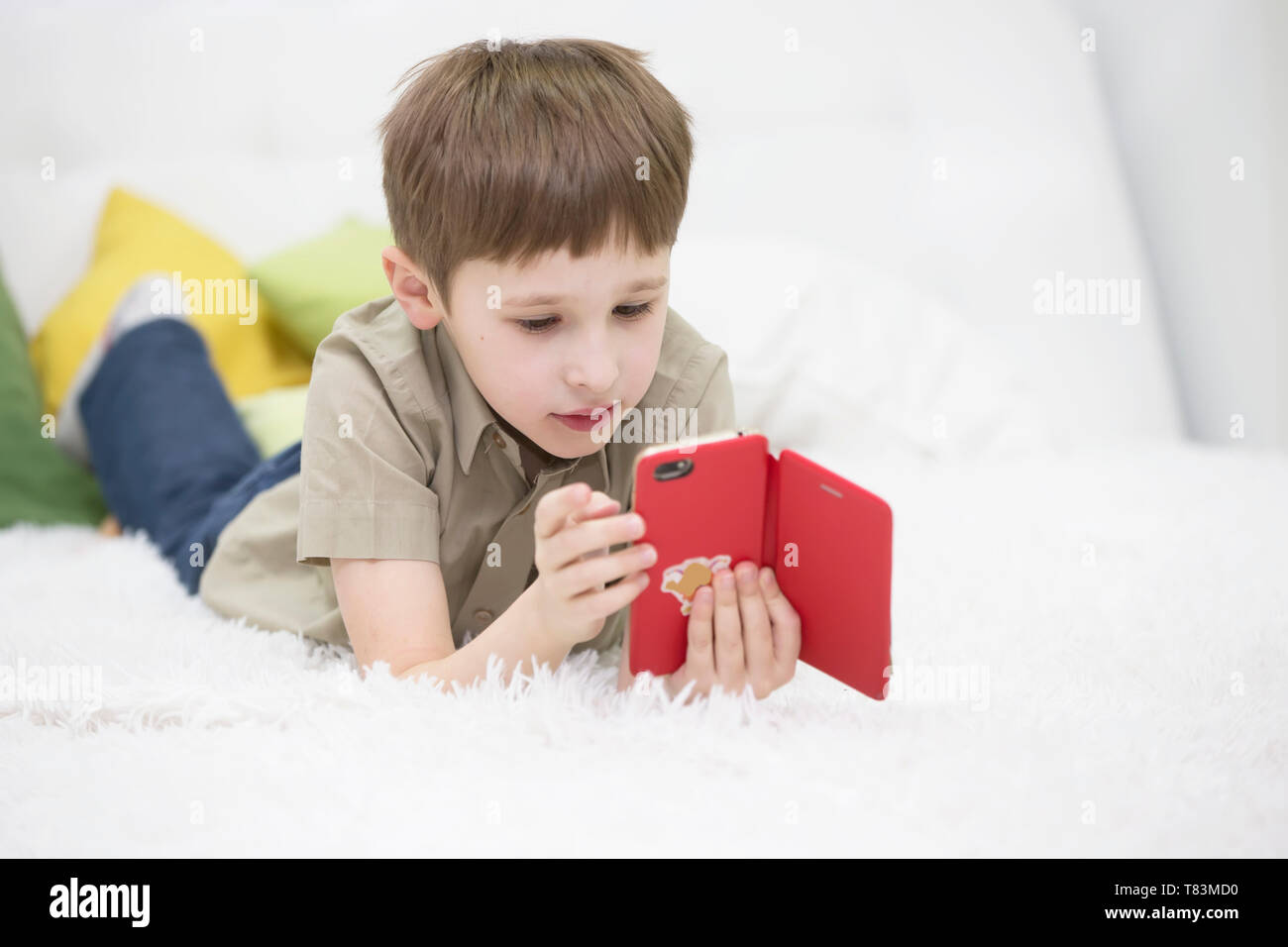 Child with a mobile phone. Schoolboy with a smartphone lying on the bed ...