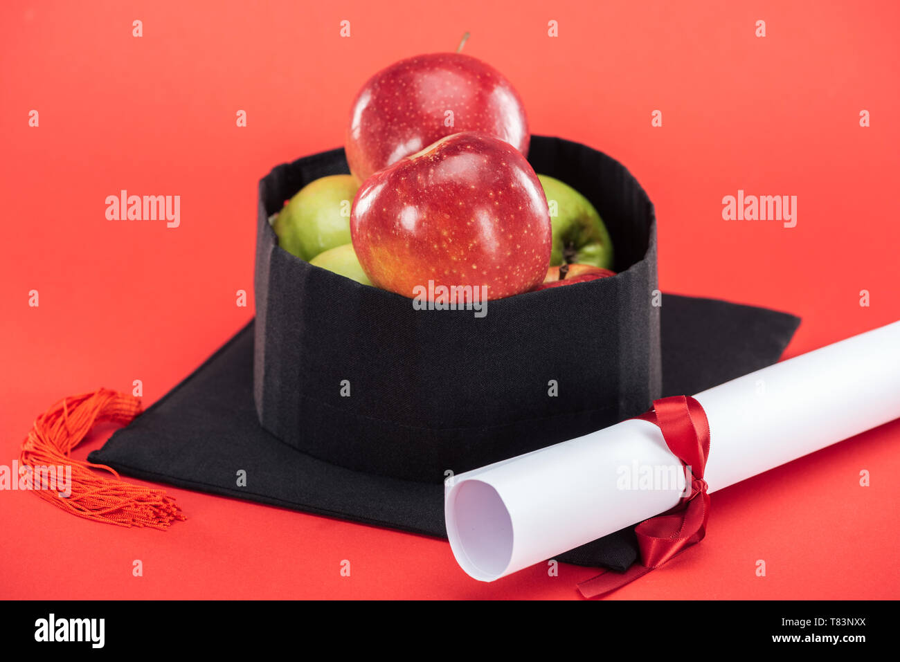 Academic cap with apples and diploma on red surface Stock Photo - Alamy