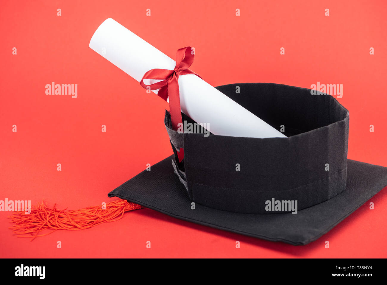 Academic cap with tassel and diploma with ribbon on red surface Stock ...