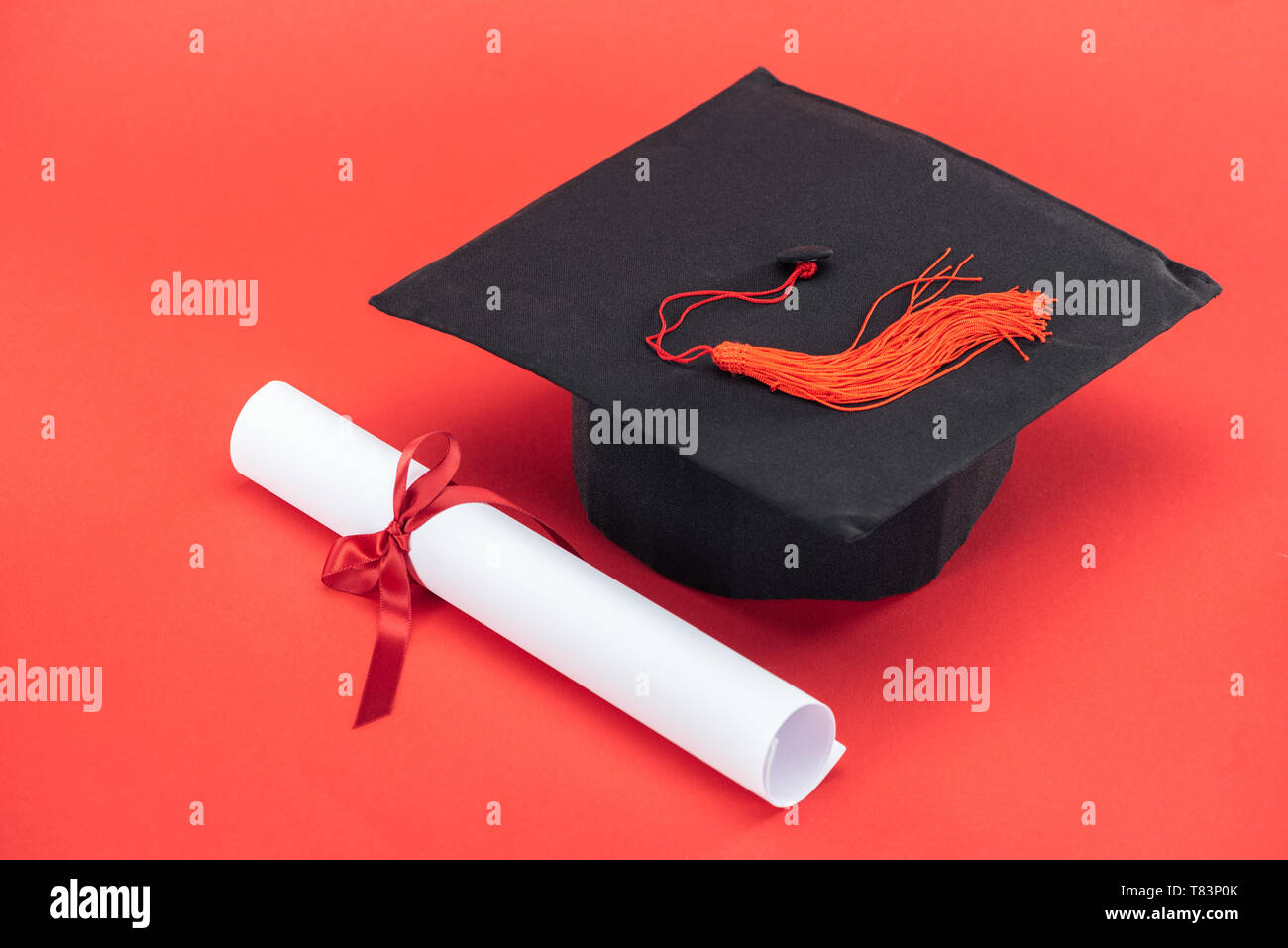 Academic cap with tassel and diploma with ribbon on red surface Stock ...