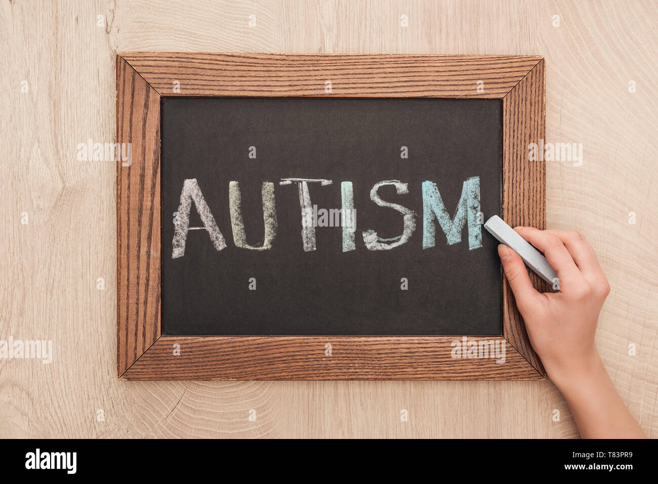 partial view of woman writing autism lettering with chalk on chalkboard ...