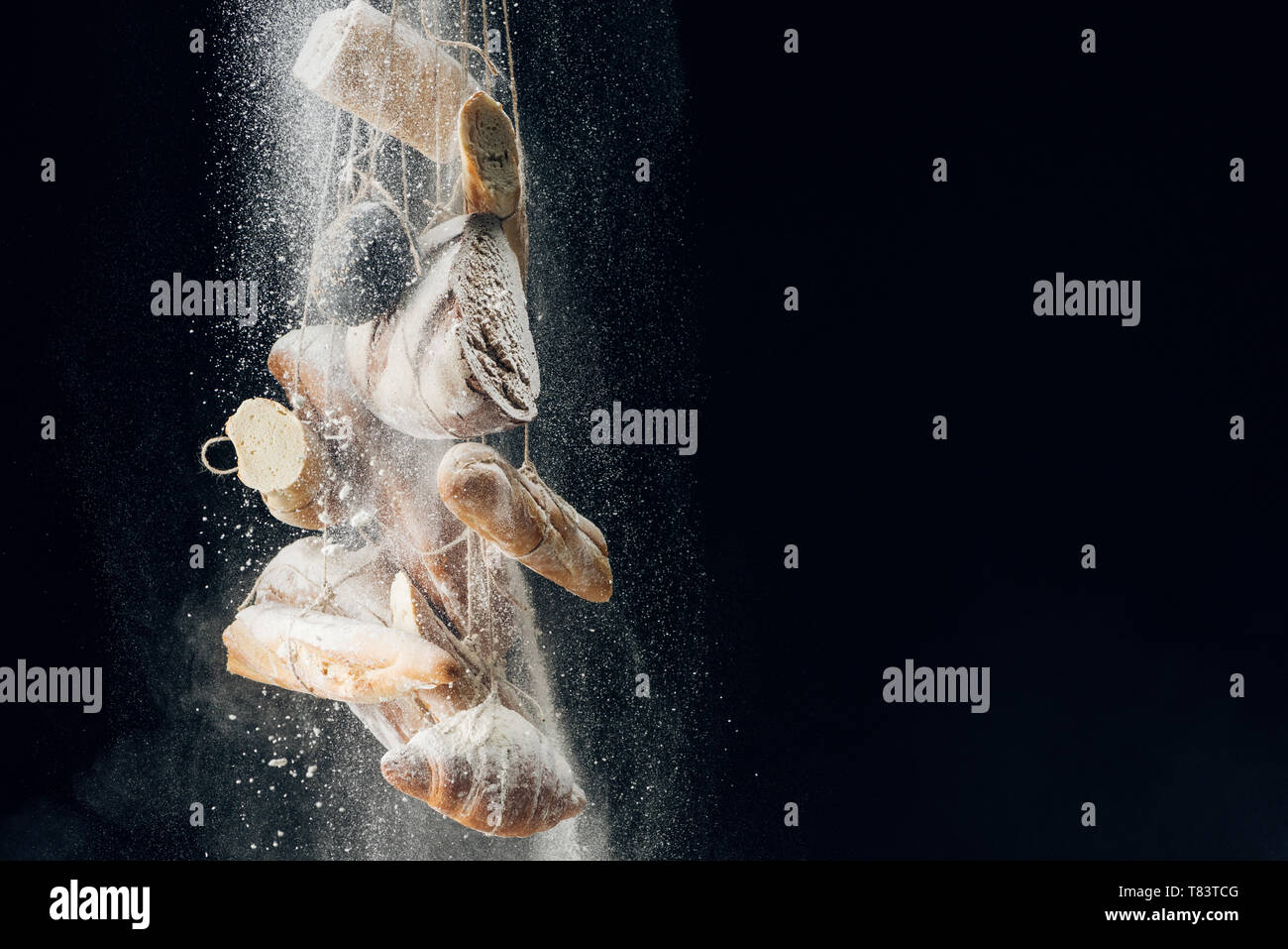 white flour falling at bread on ropes on black background with copy ...