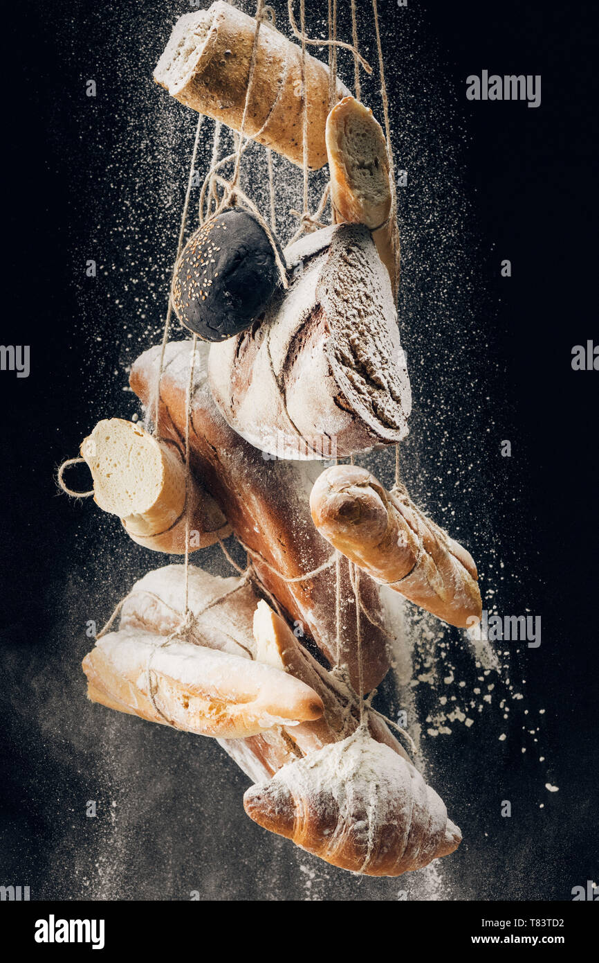 white flour falling at bread, baguettes and croissant on ropes on black ...