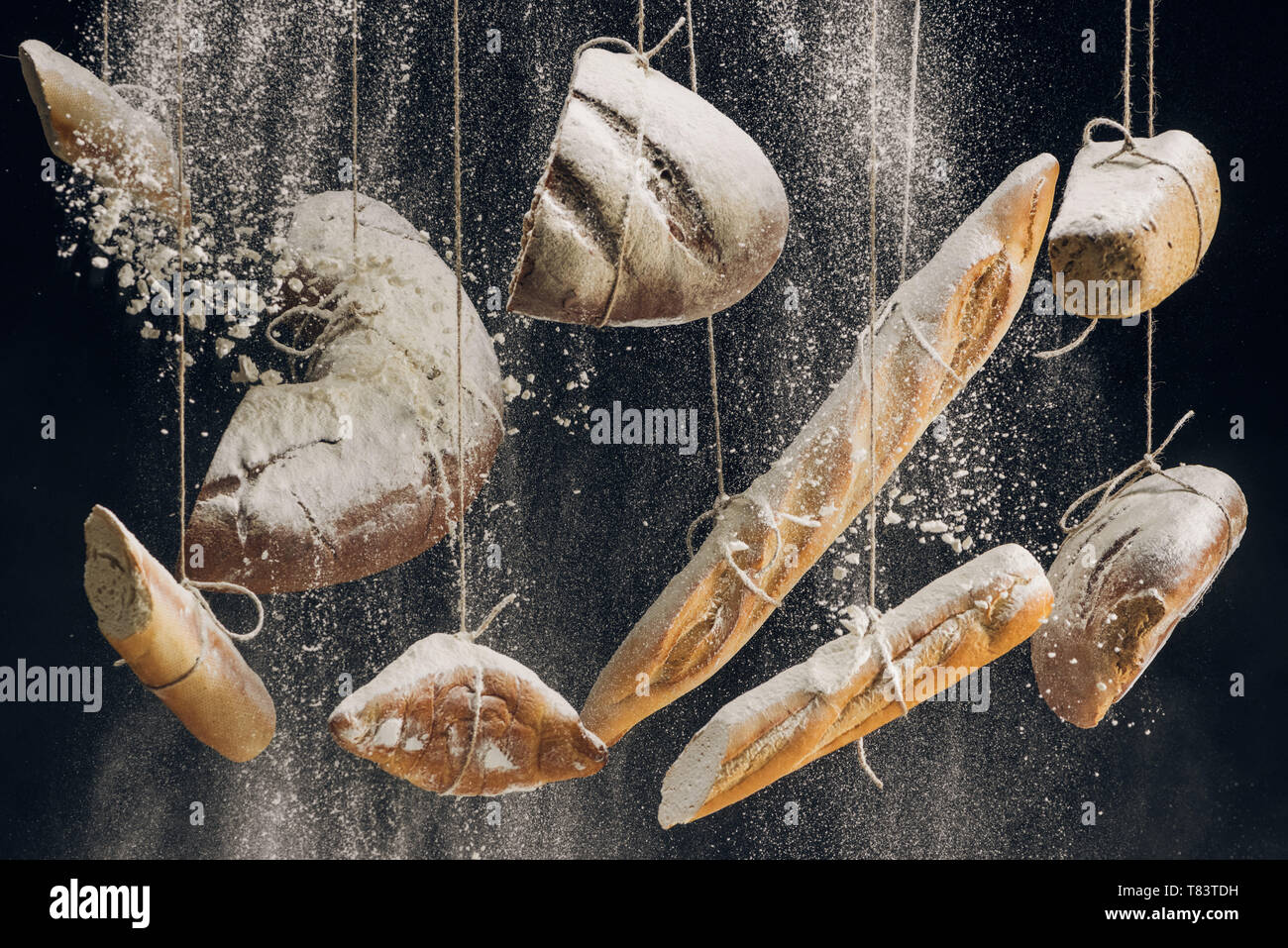 flour falling at fresh baked bread hanging on ropes on black background ...