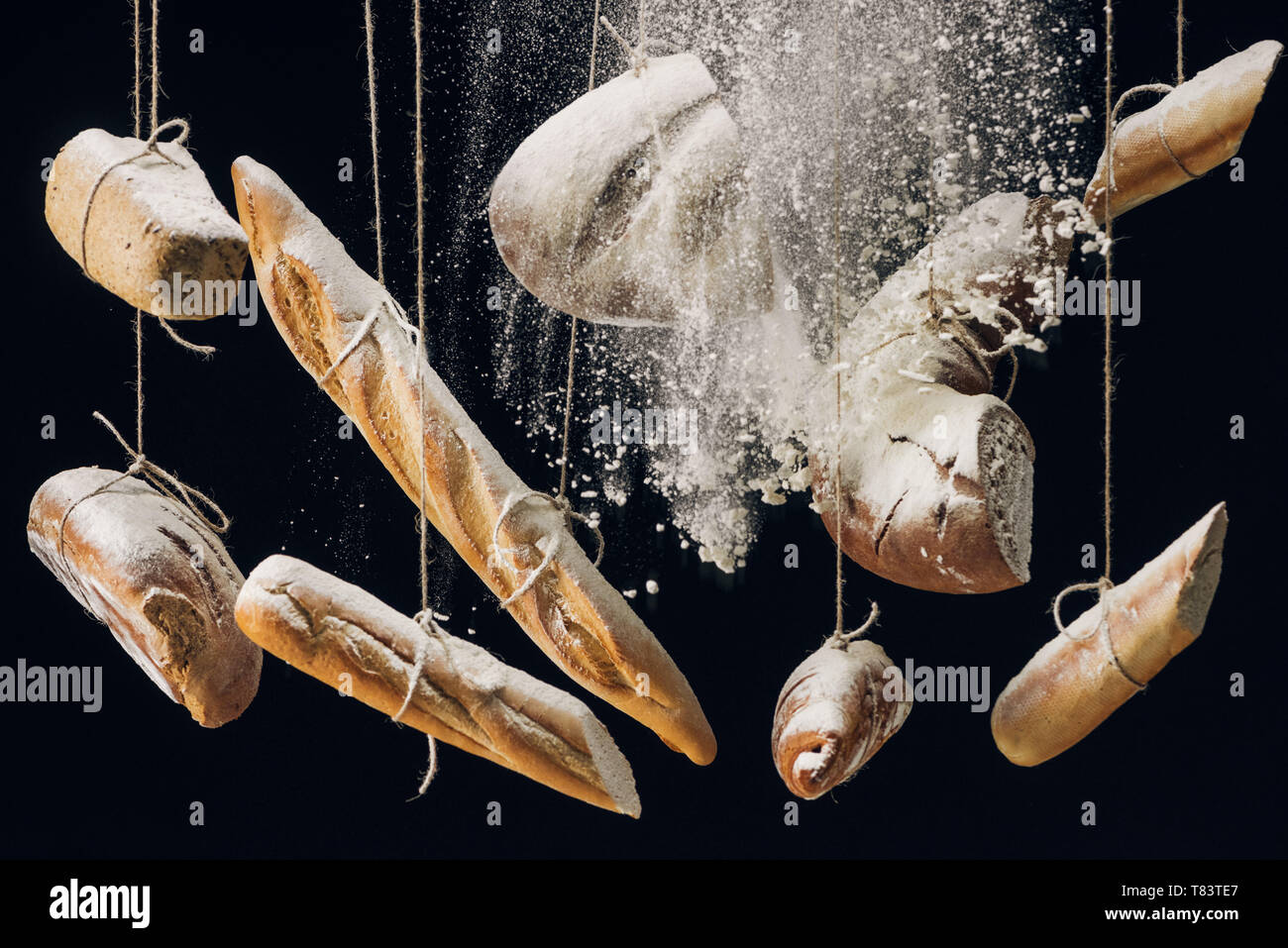 white flour falling at fresh baked bread hanging on ropes on black ...