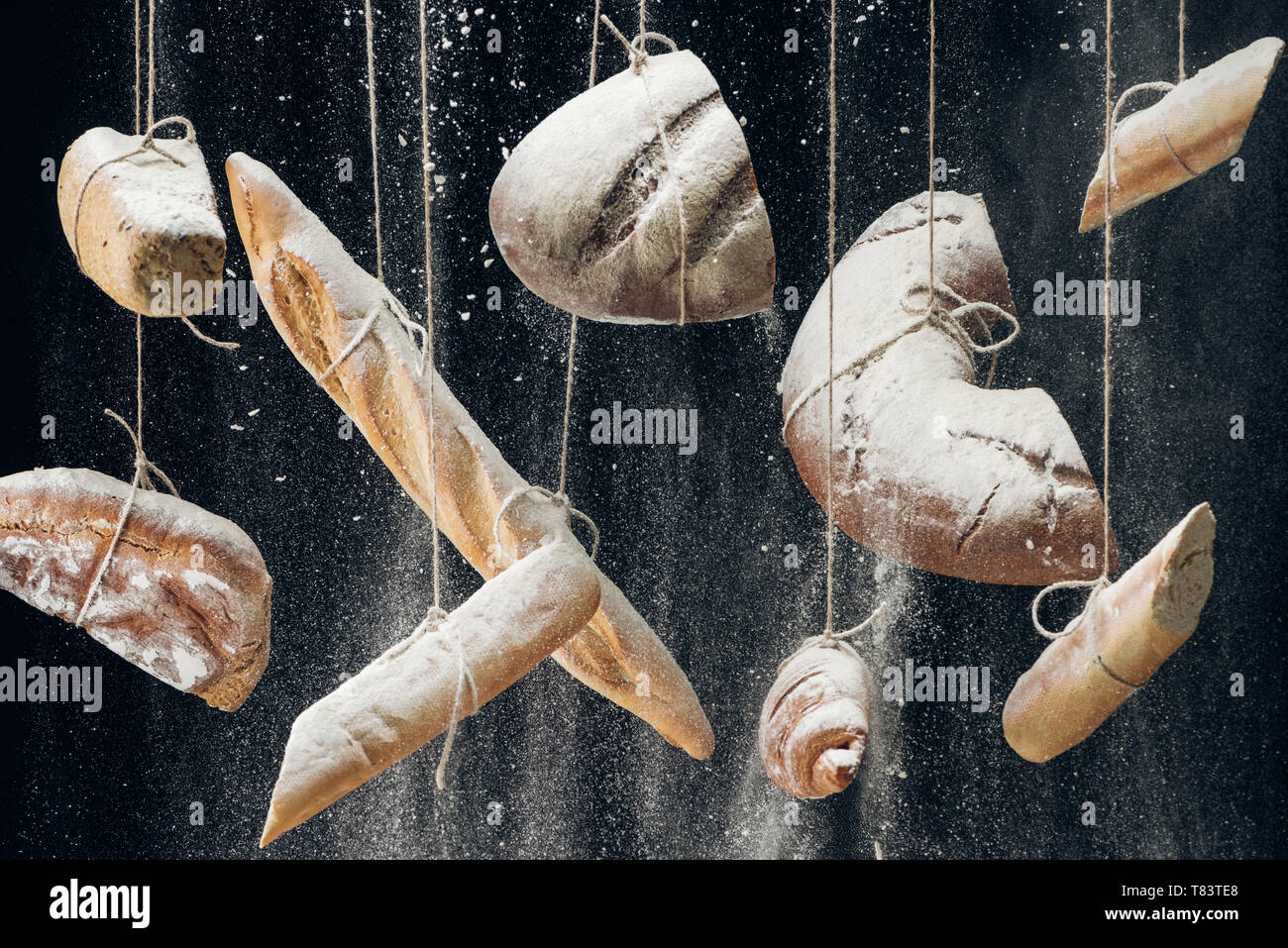 white flour falling at baked bread, baguettes and croissant hanging on ...