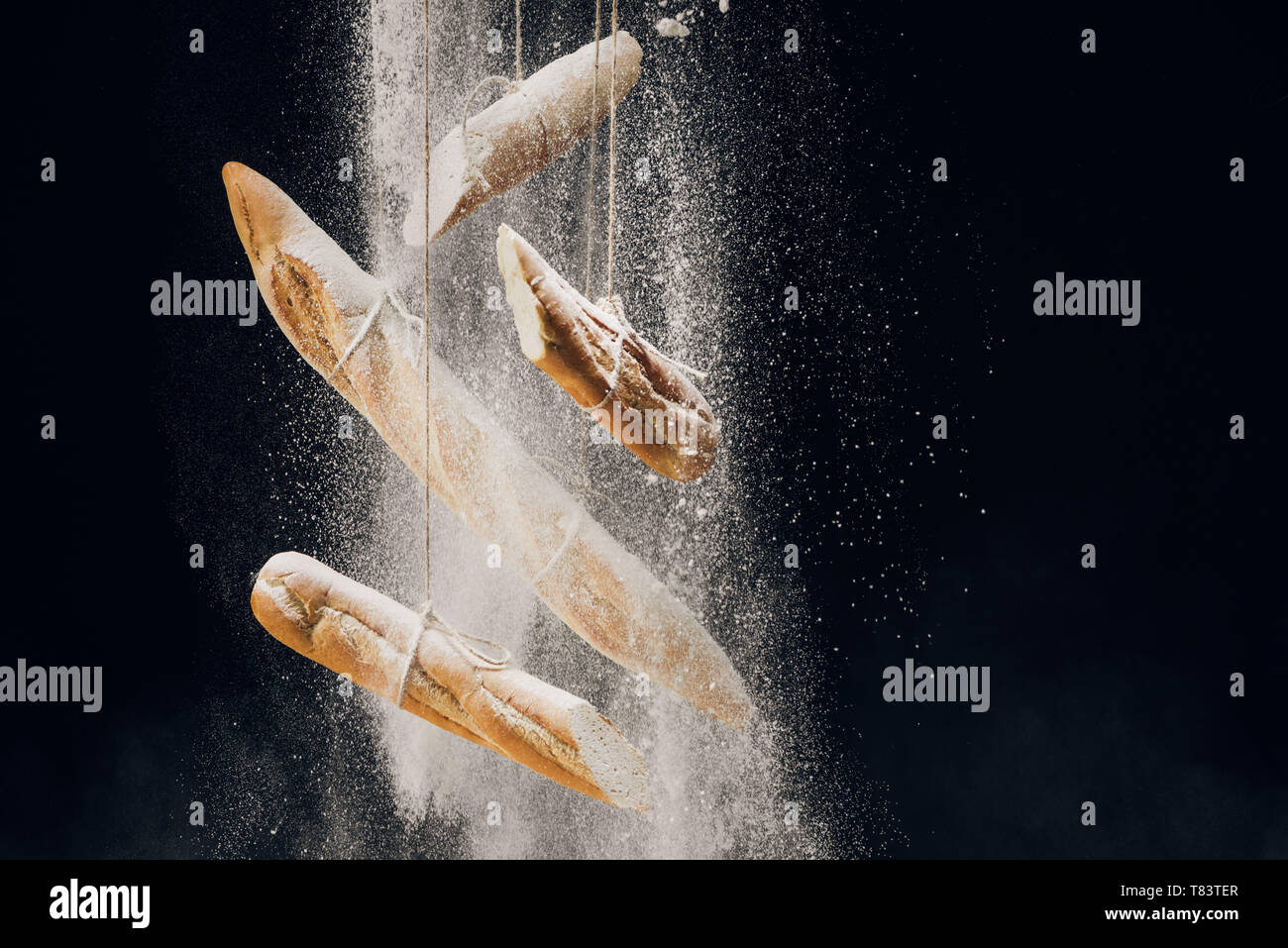 white flour falling at loaves of fresh baked baguettes on ropes on ...