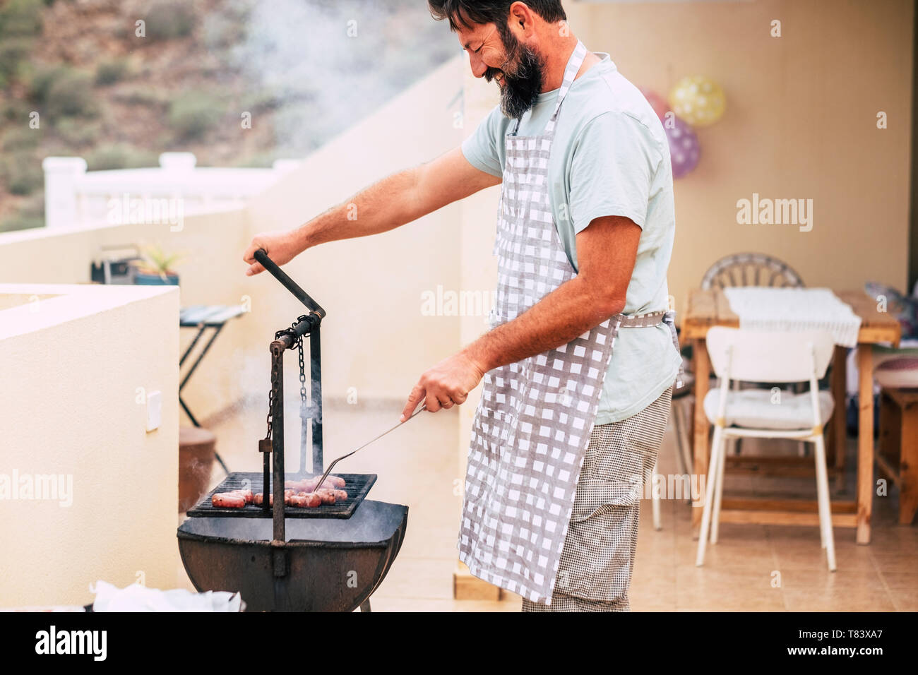 Happy adult man with beard cooking meat with grill barbecue at home for ...