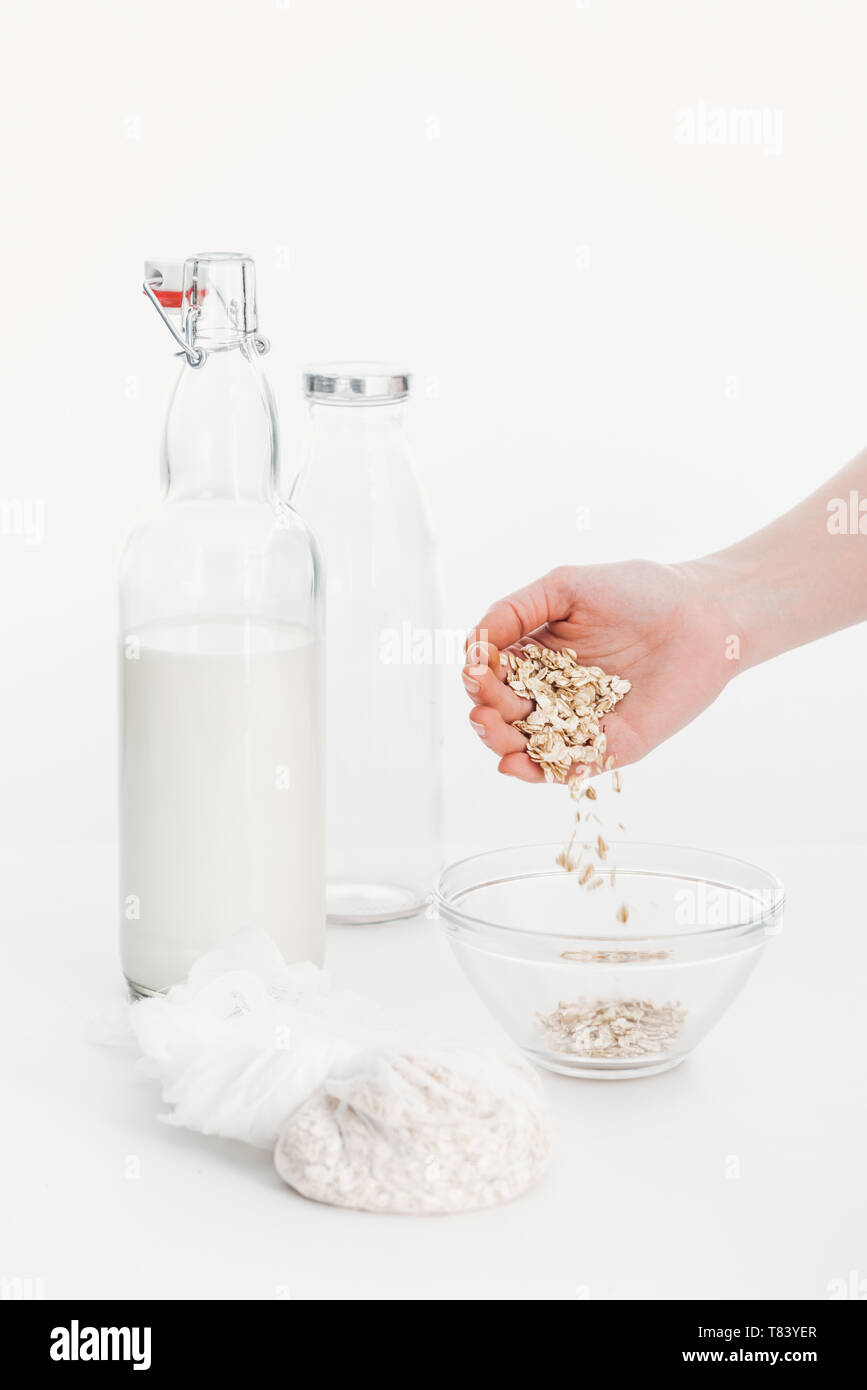 cropped view of woman putting oat flakes in bowl while cooking oat ...