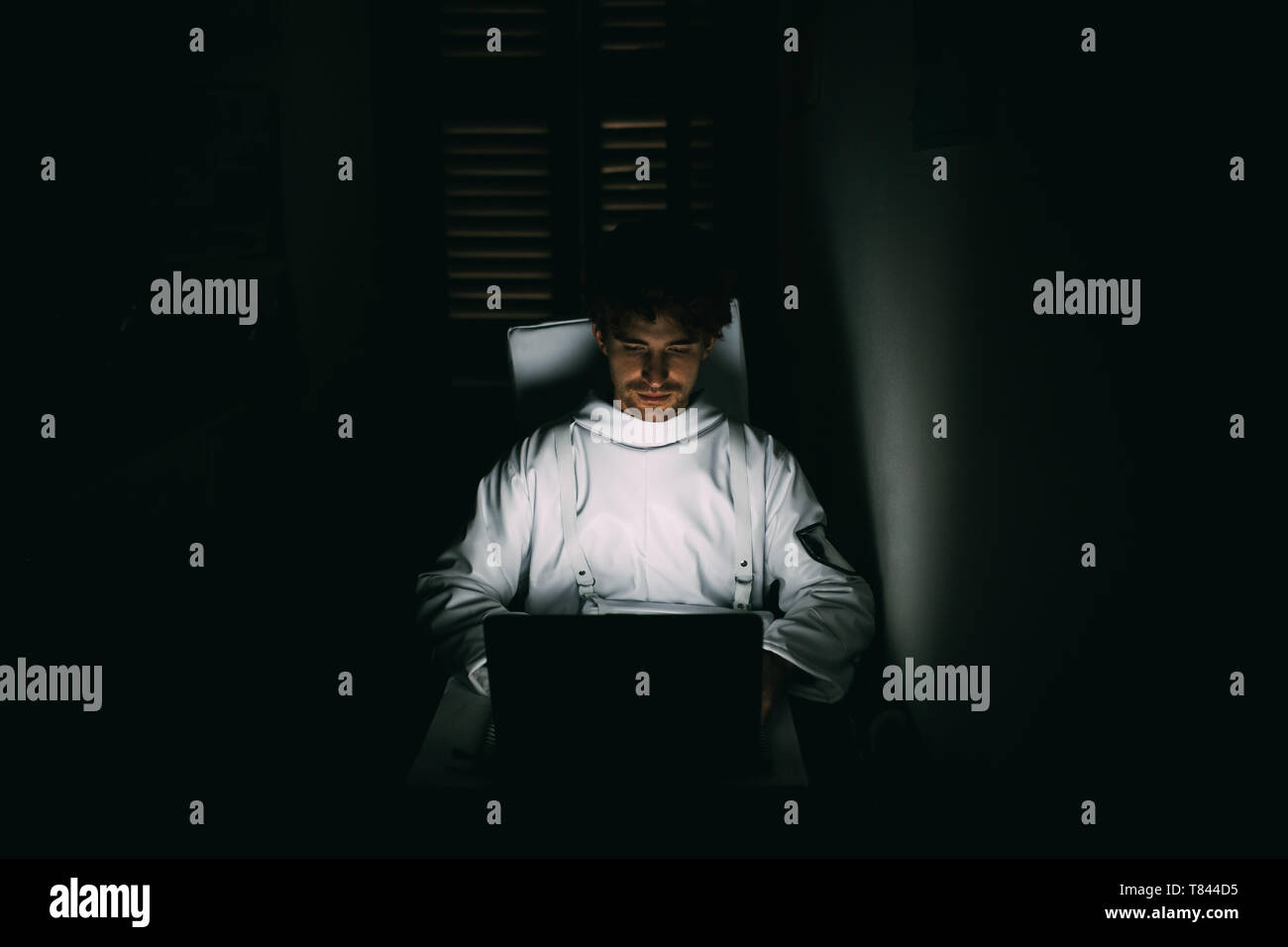 Astronaut using laptop in dark room Stock Photo - Alamy