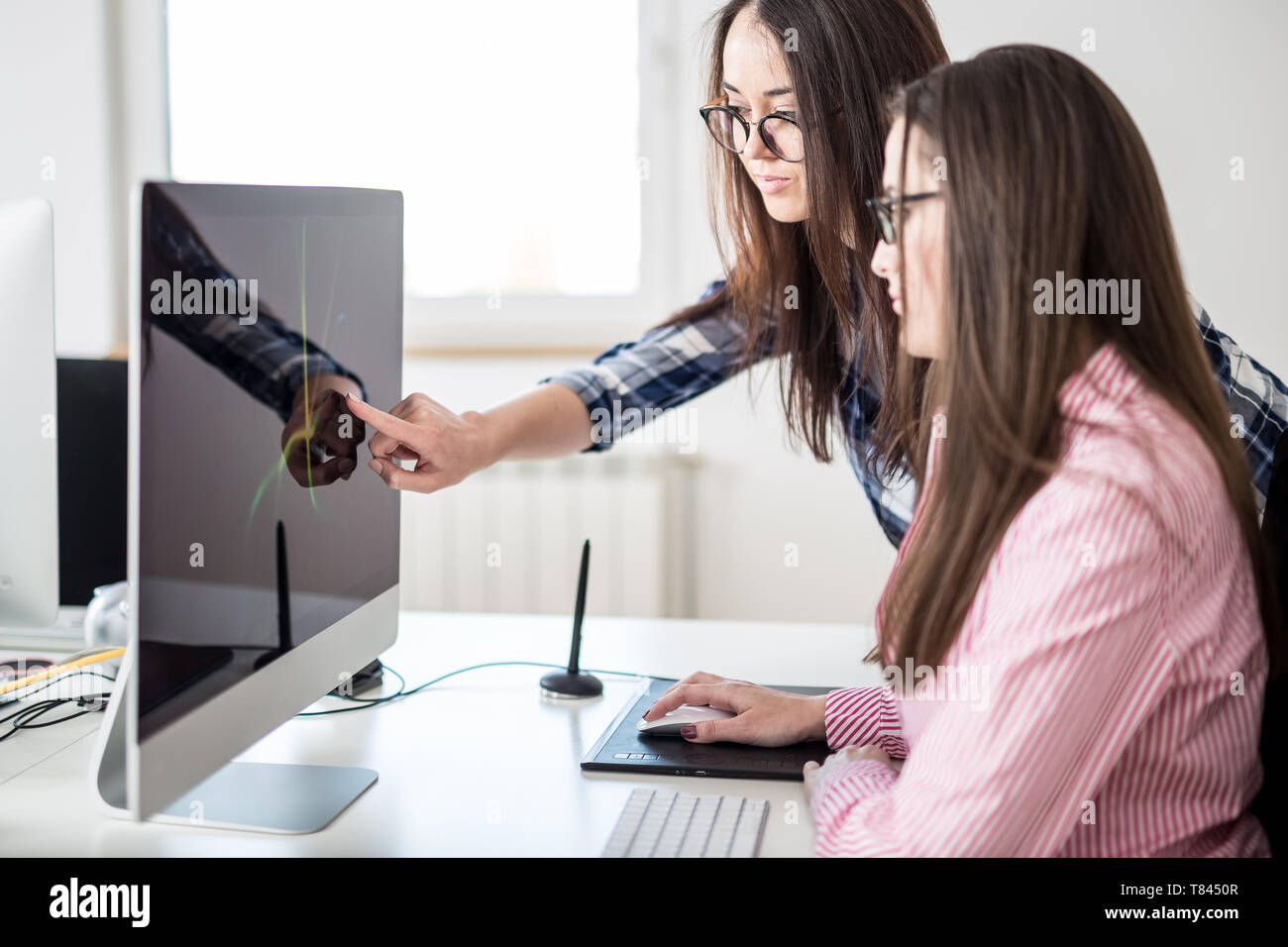 Two cheerful fashionable females looking and showing something on ...