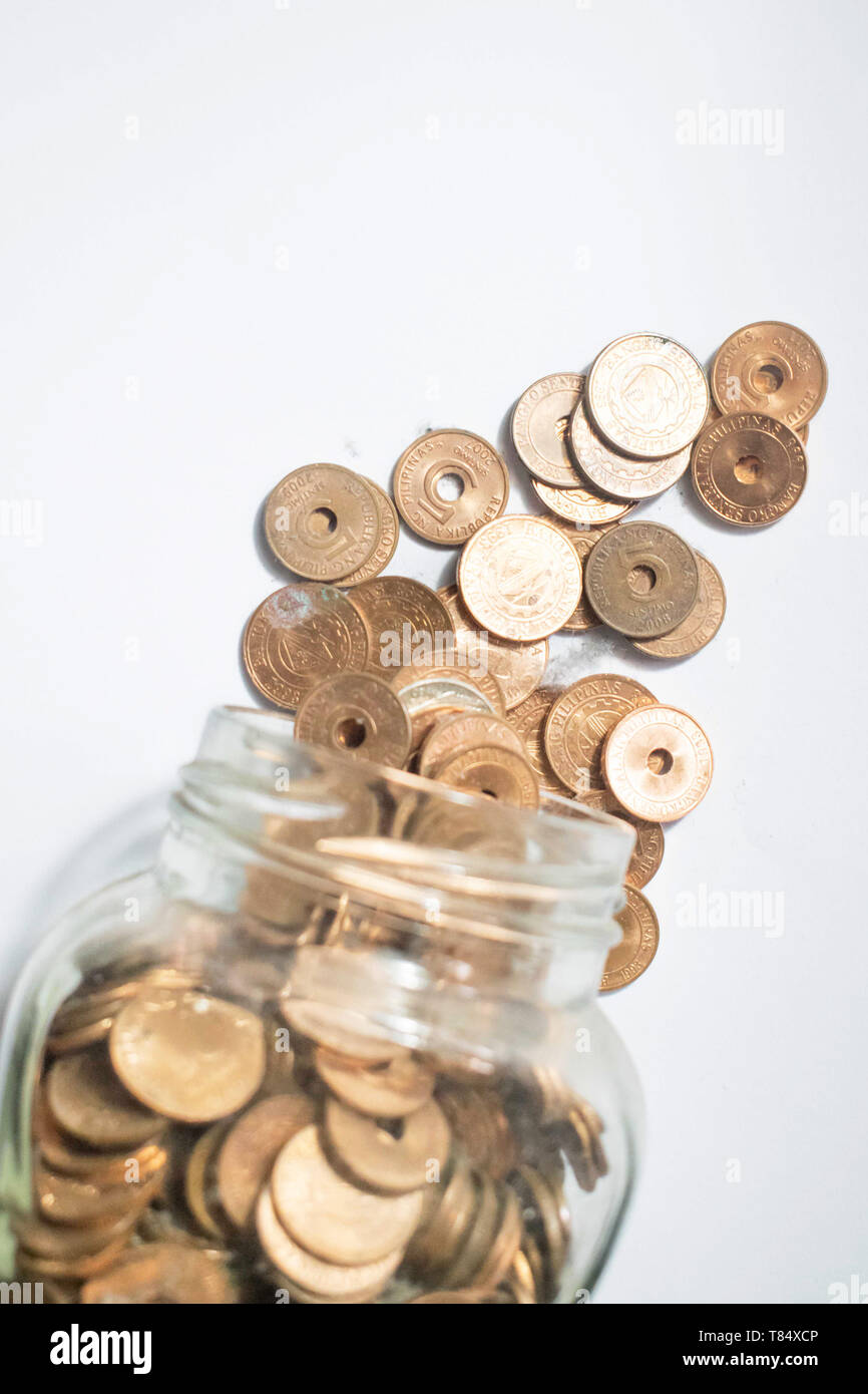 Coins coming out of a glass jar, glass jar laying on a white background ...