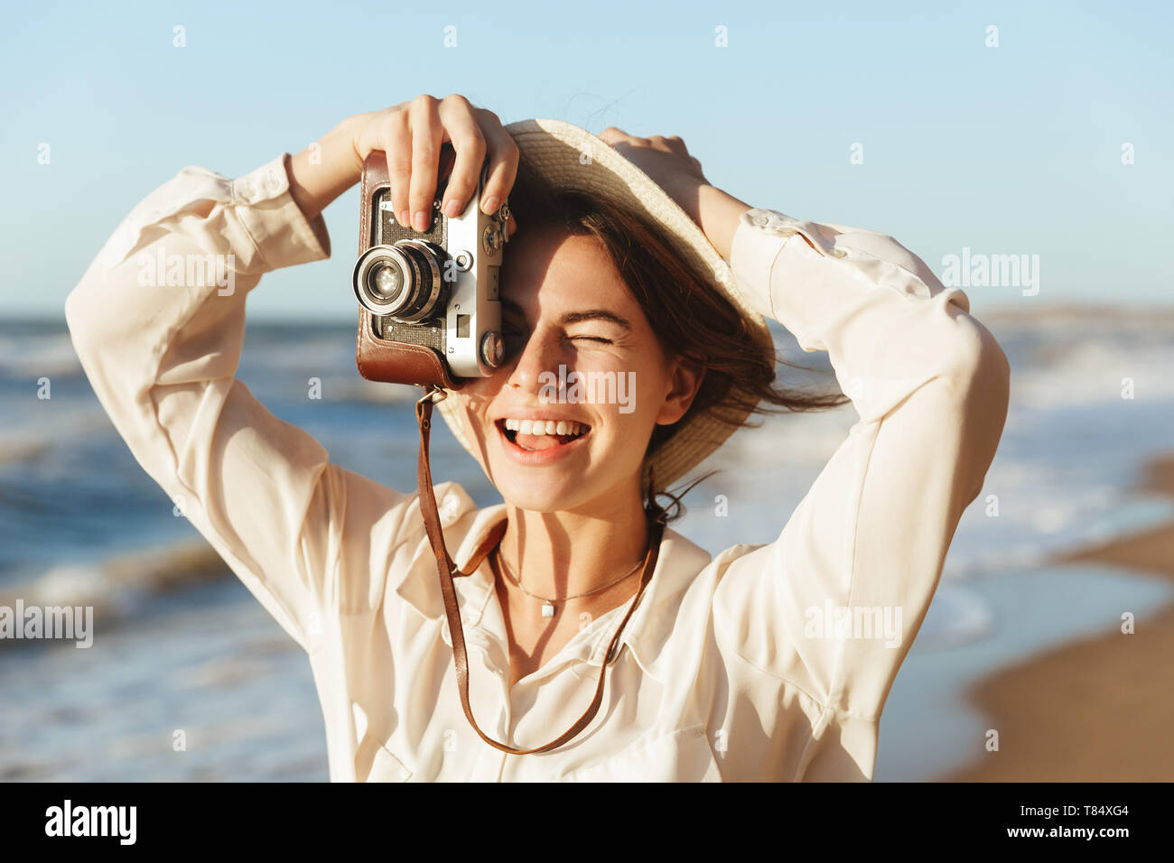 Image of excited woman 20s photographing on retro camera while walking ...