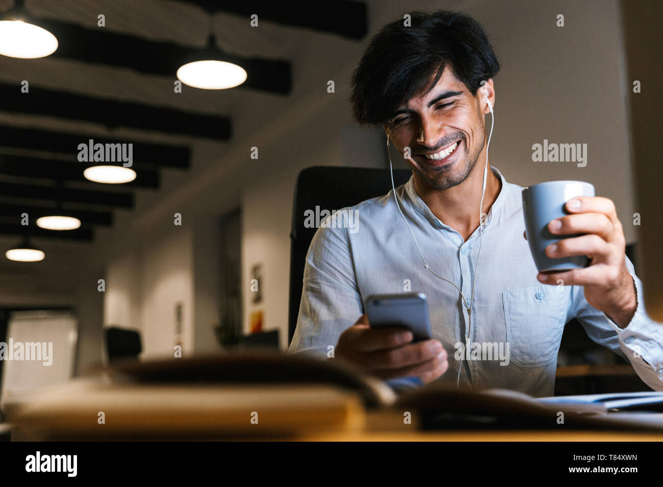 Smiling young man working at the office late at night, using computer ...