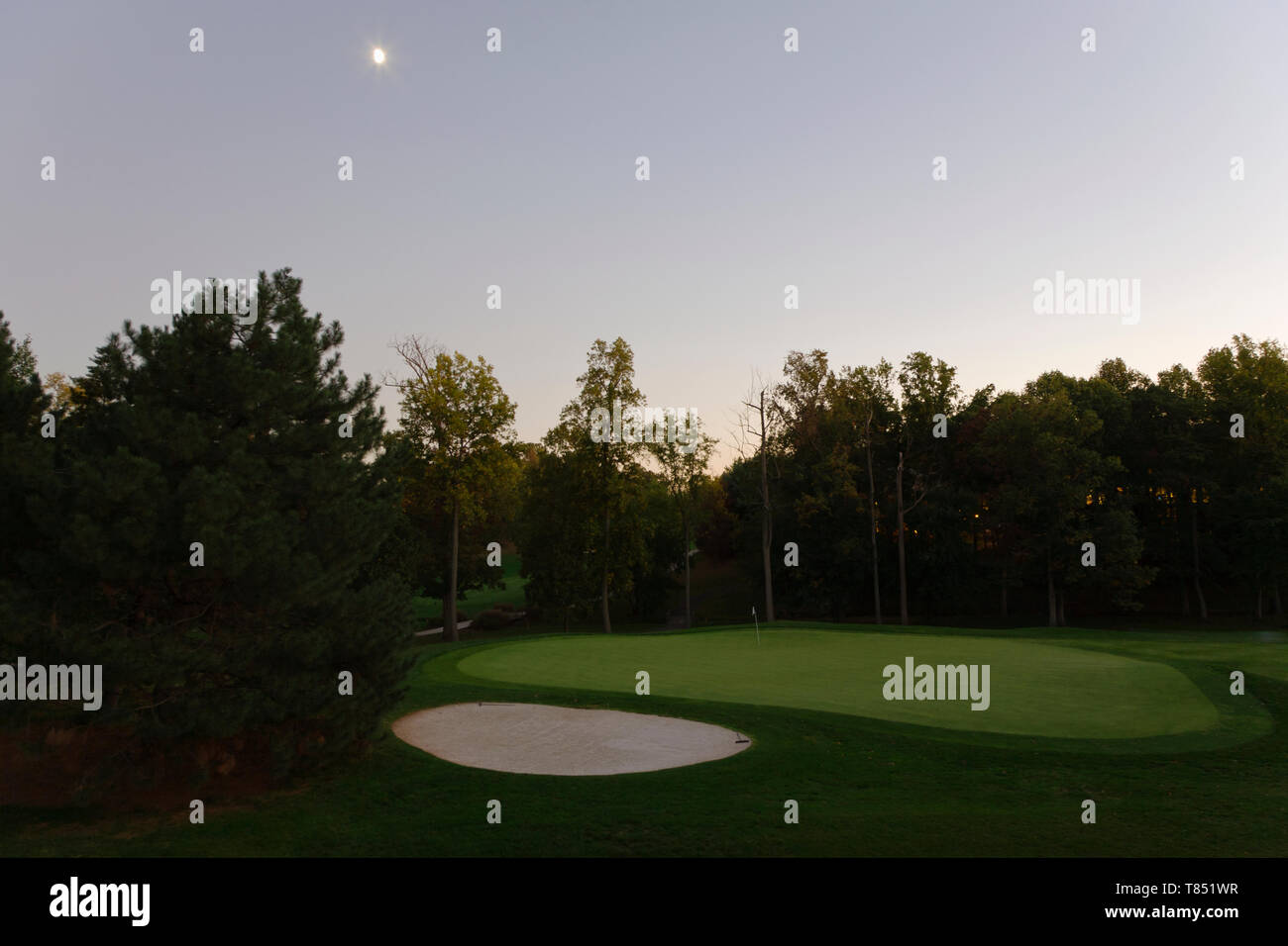 A full moon in the sky at dusk, hanging over a sand trap on a golf ...
