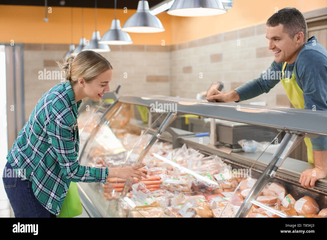 Male seller helping woman to choose meat products in butcher shop Stock ...