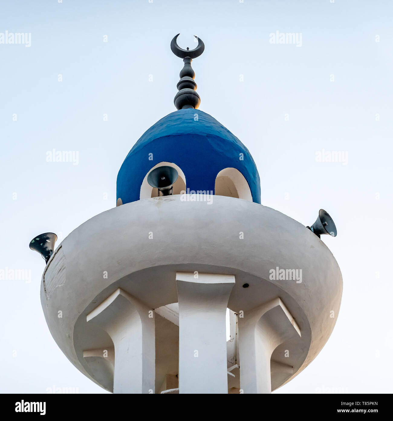 White and blue painted tip of a minaret with loudspeakers and a bronze ...