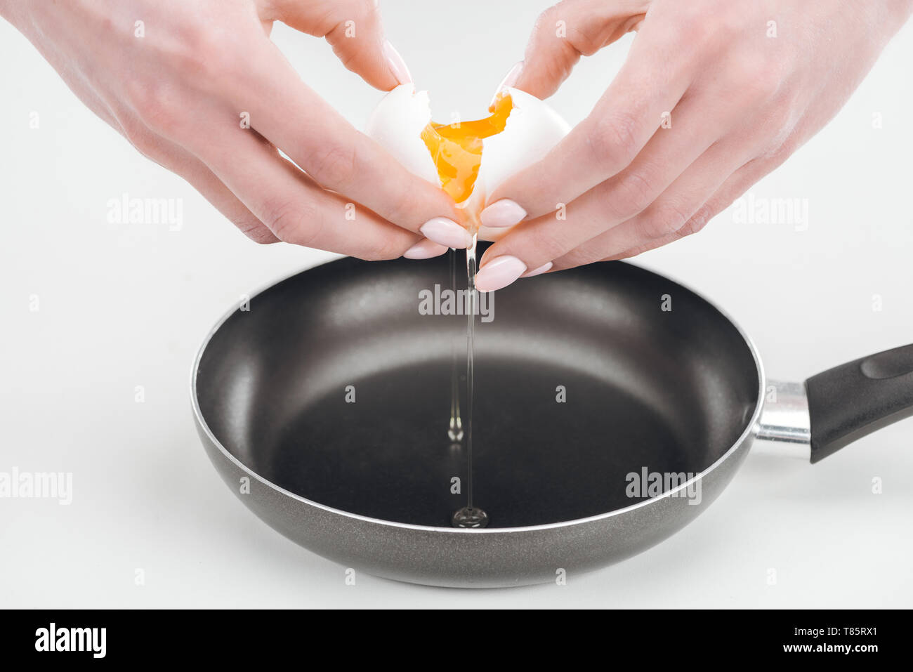 partial view of woman smashing egg with hands into pan on white ...
