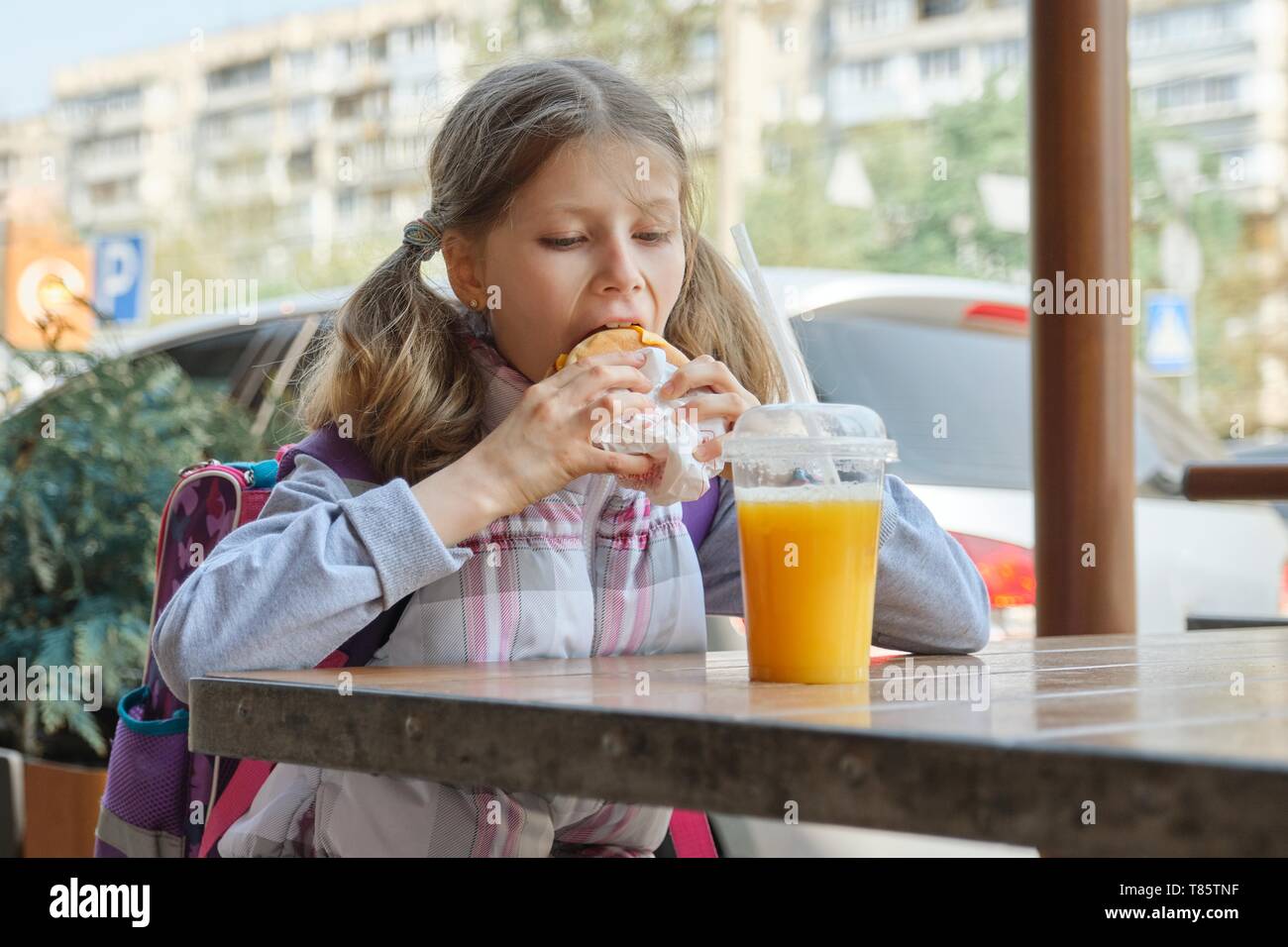 Portrait of girl student with backpack, eating burger with orange juice ...
