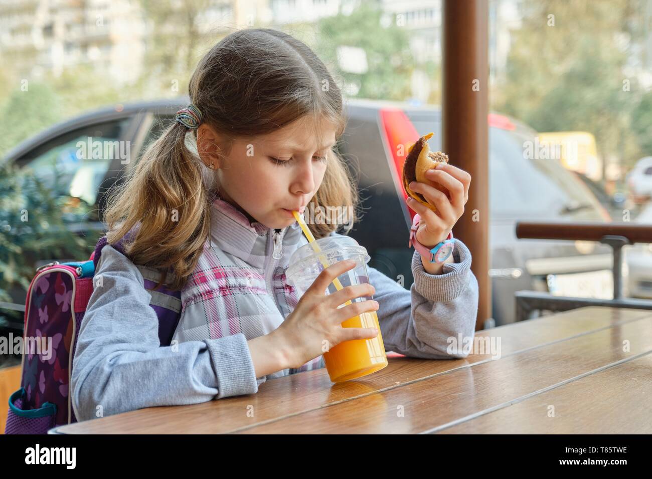 Portrait of girl student with backpack, eating burger with orange juice ...