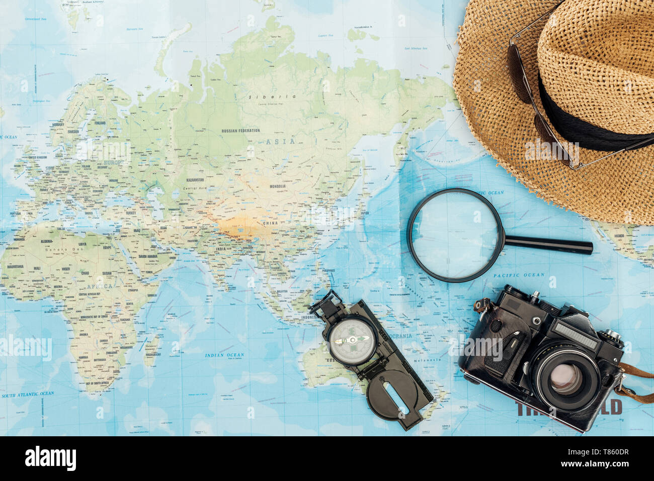 Top view of straw hat, compass, magnifier and film camera on world map ...
