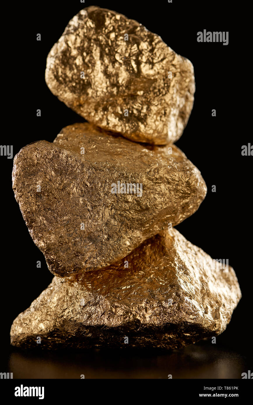 close up view of three gold textured shiny stones isolated on black ...