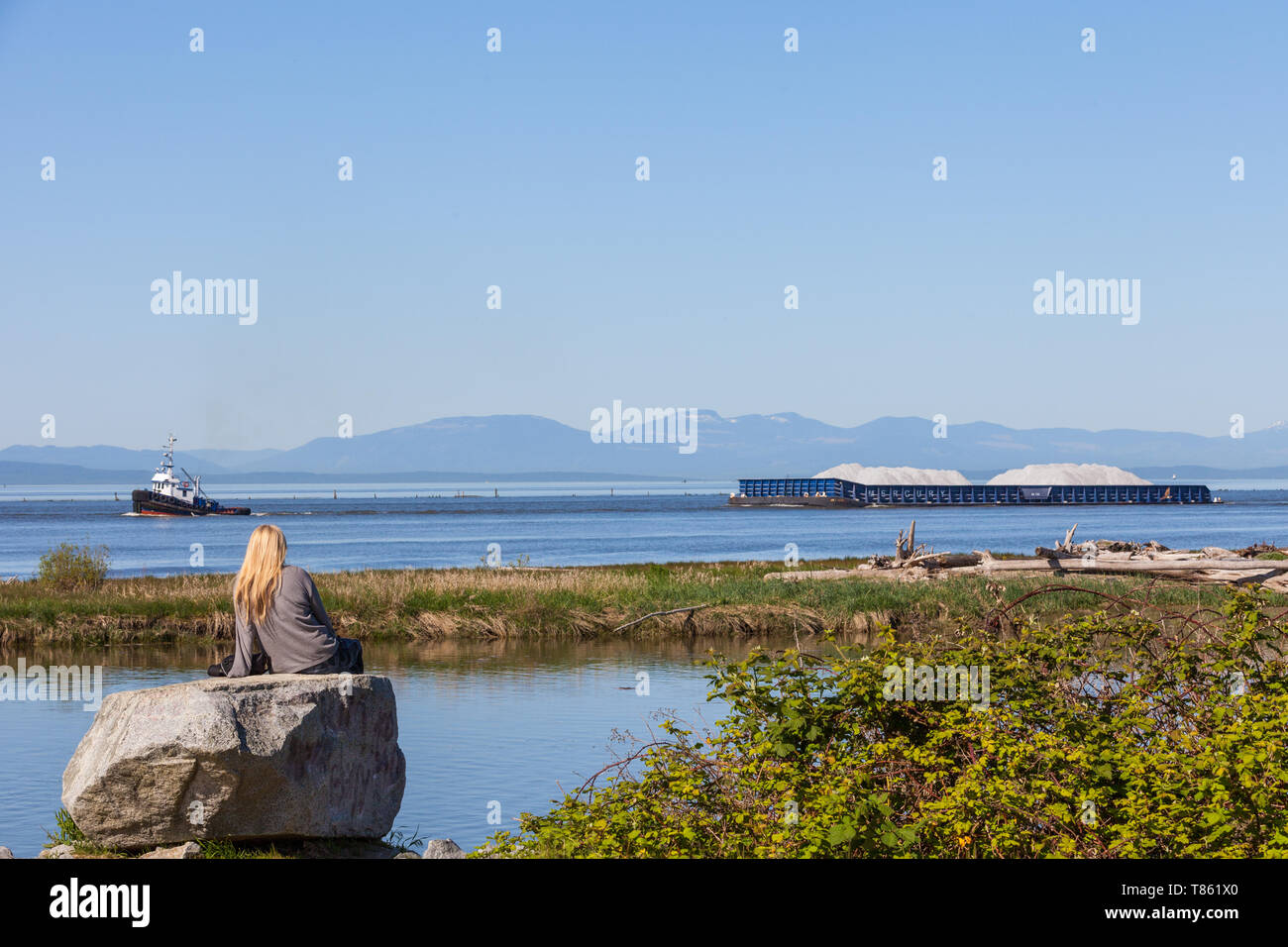 Young woman sitting on a rock in Gary Point park Steveston watching a ...