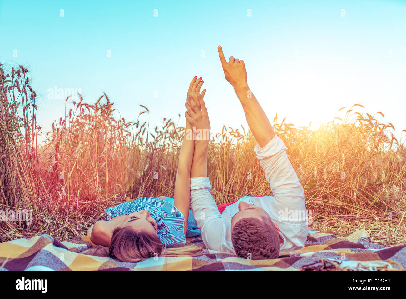 A young couple, man woman, in wheat field summer, lie on rug. Hand ...