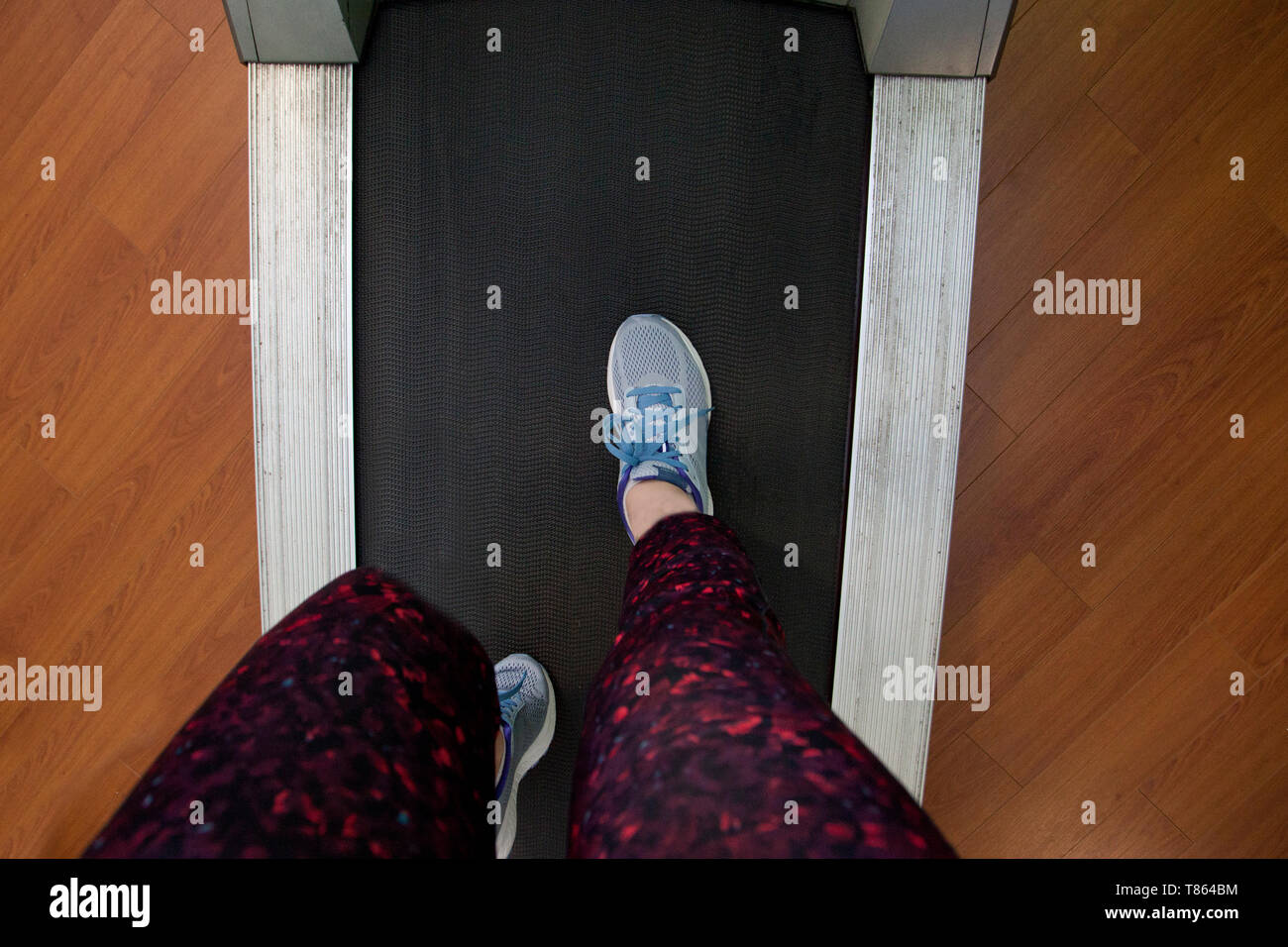 Looking down at a pair of legs and sneakers ready to run on a treadmill ...