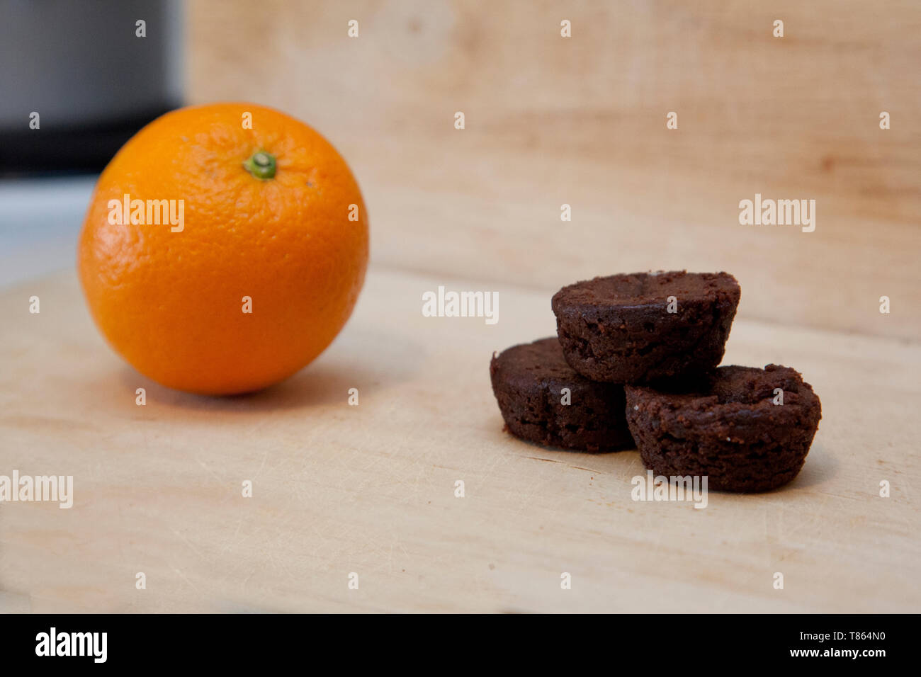 An orange and a small stack of brownies together on a kitchen cutting ...