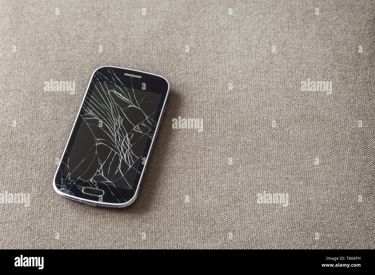Black old cellphone with cracked screen on light cloth copy space ...