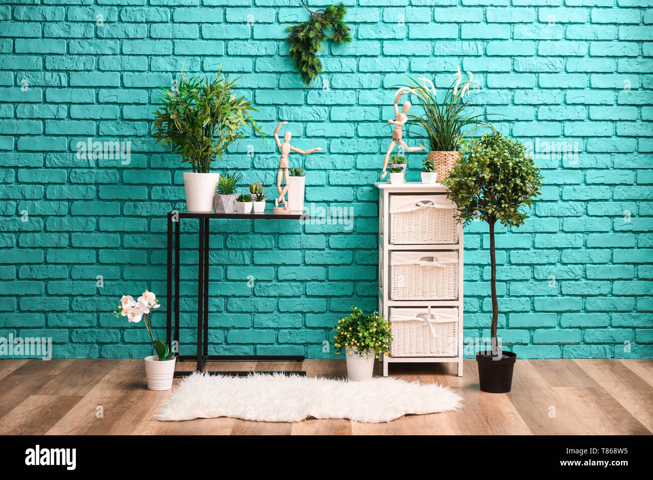 Stylish stand with with wicker baskets, table and plants near color ...