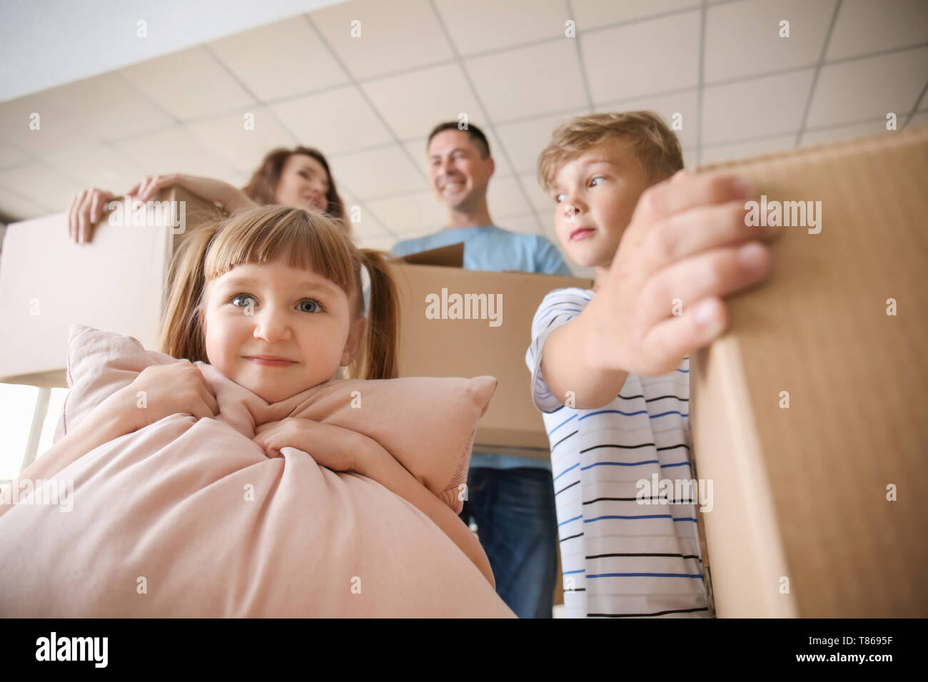 Children and their parents with boxes indoors. Moving into new house ...
