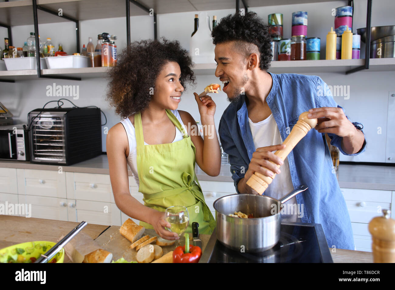 Young African-American couple tasting food while cooking together in ...
