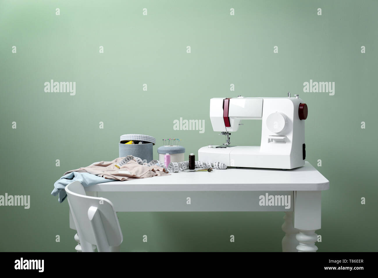 Sewing machine with tailor's accessories on table against color ...
