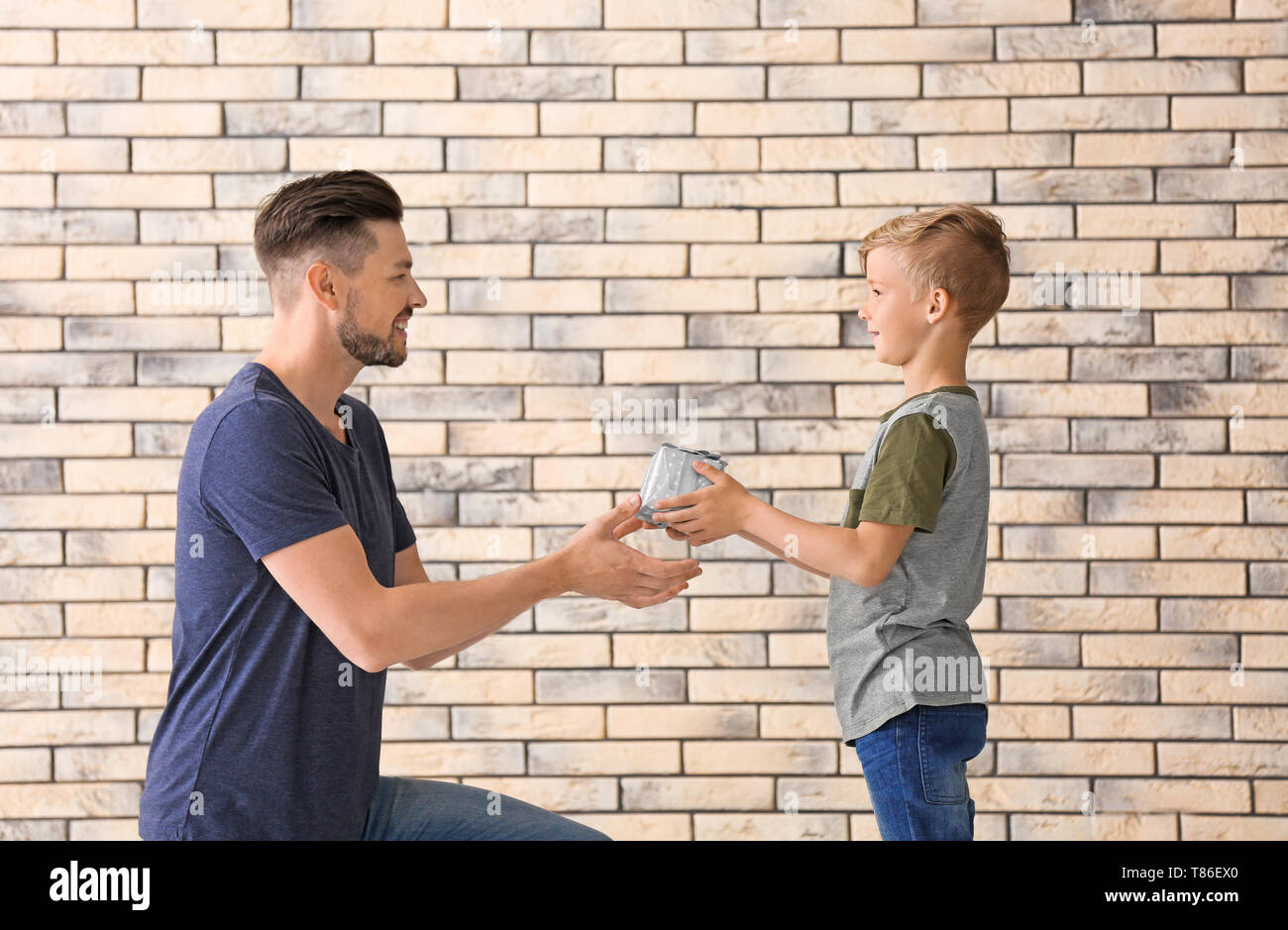 Man receiving gift for Father's Day from his son on brick wall ...