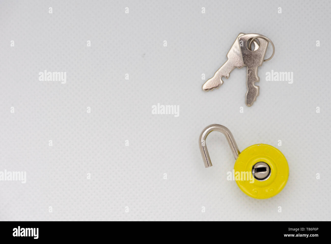 Silver keys and a yellow unlocked padlock on an isolated white ...