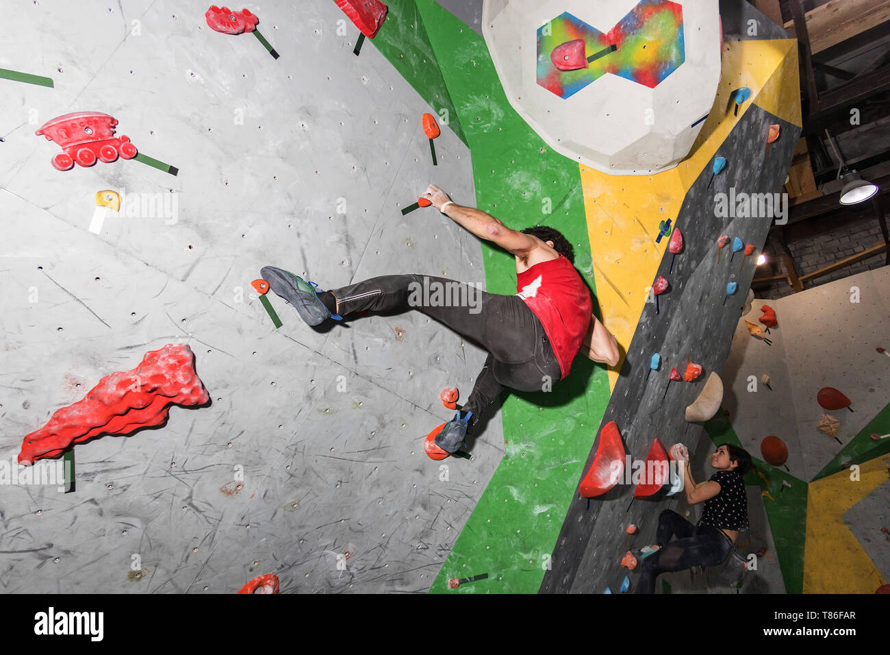 Rock climber man hanging on a bouldering climbing wall, inside on ...