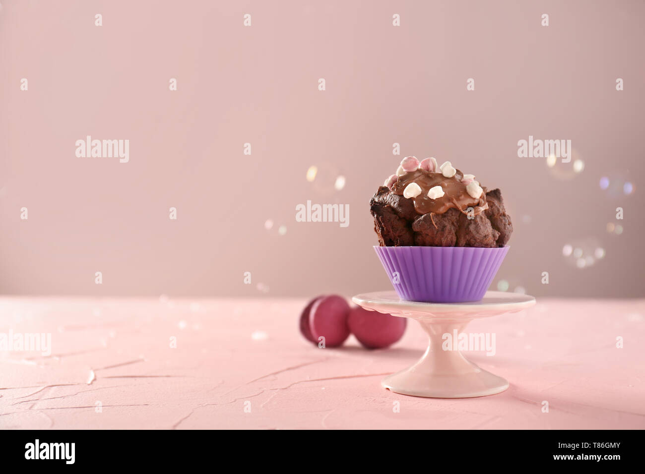Dessert stand with delicious cupcake on table against color background ...