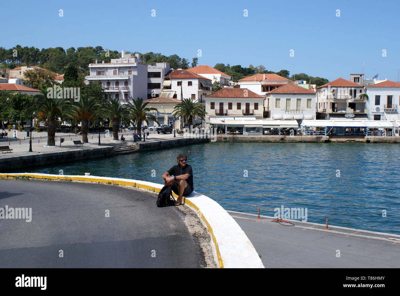 Man sitting on roadside next to Pylos harbour, Pylos, Greece Stock ...