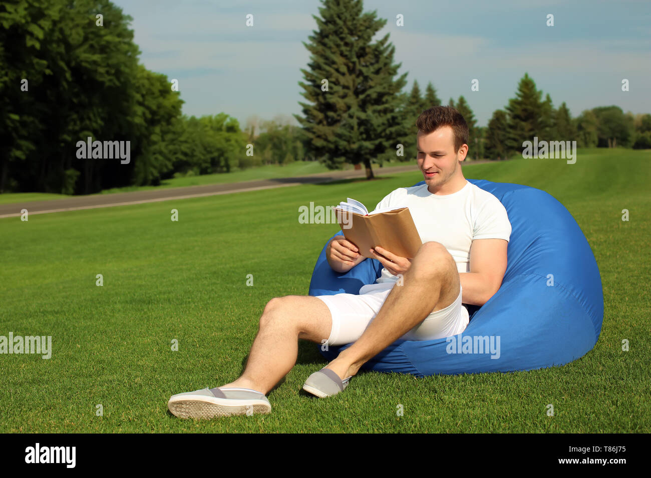 Young man reading book while sitting on bean bag chair outdoors Stock ...