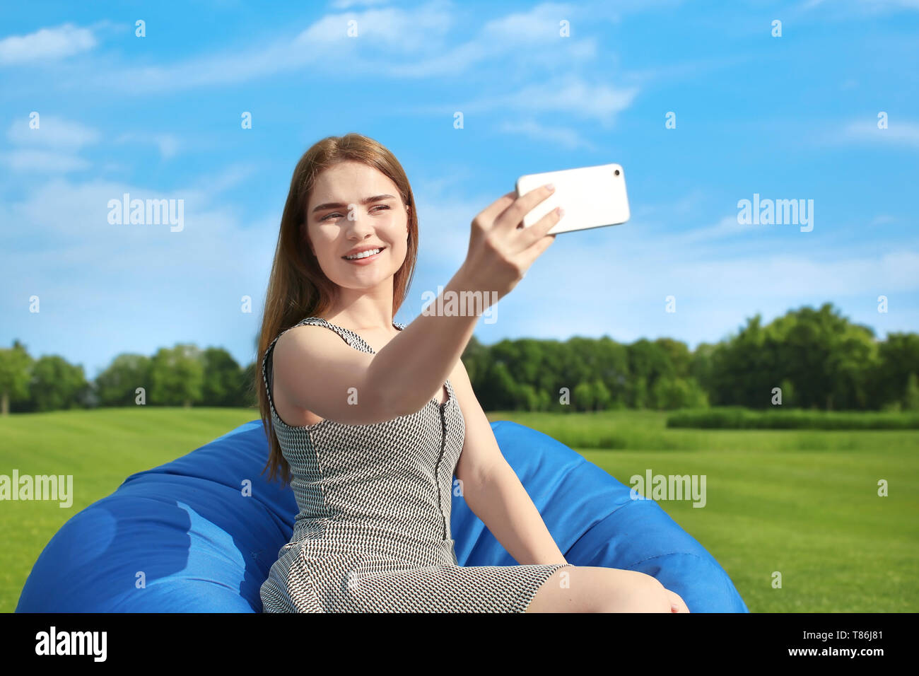 Young woman taking selfie while sitting on bean bag chair outdoors ...
