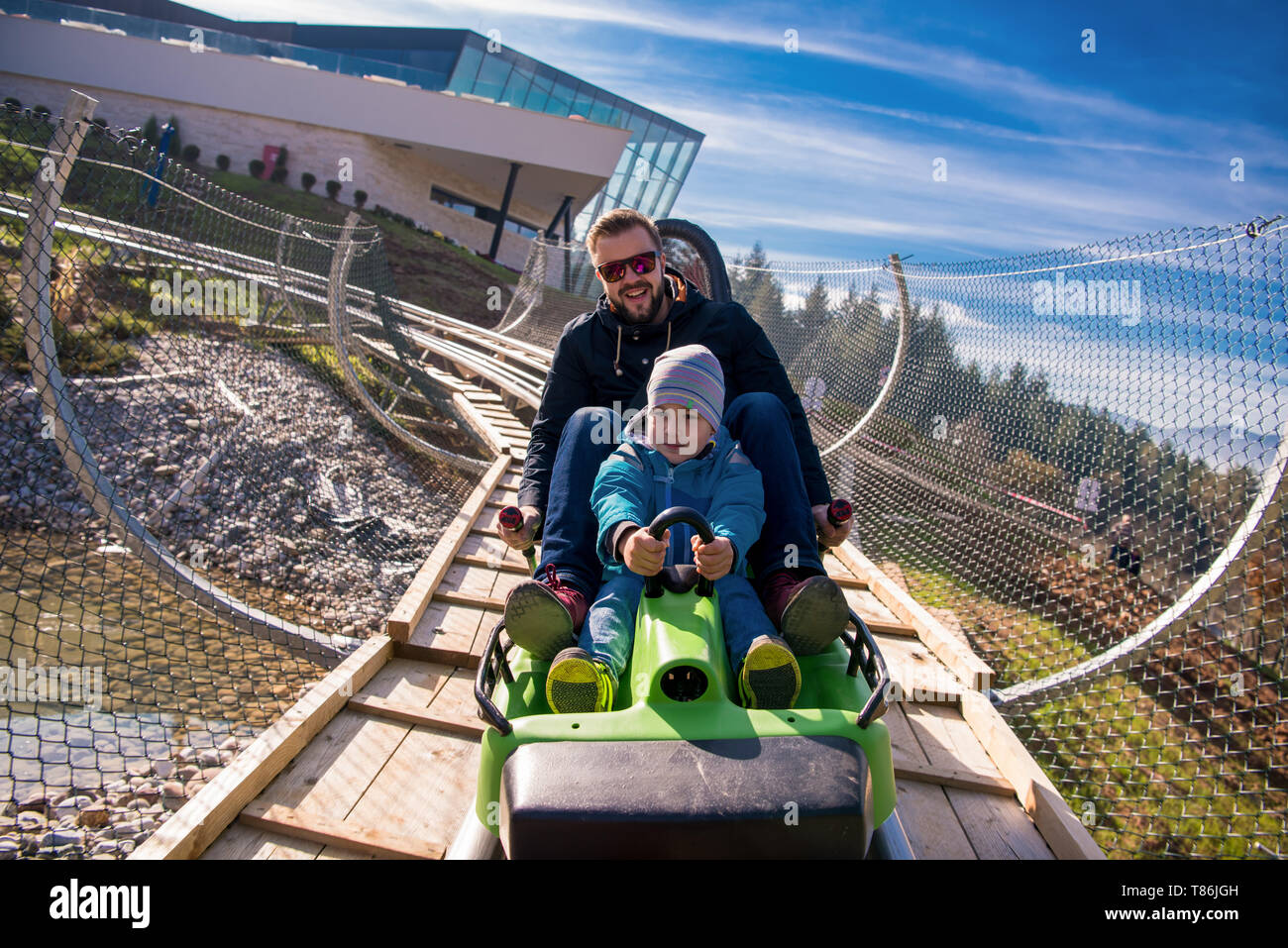 Excited young father and son driving on alpine coaster while enjoying ...