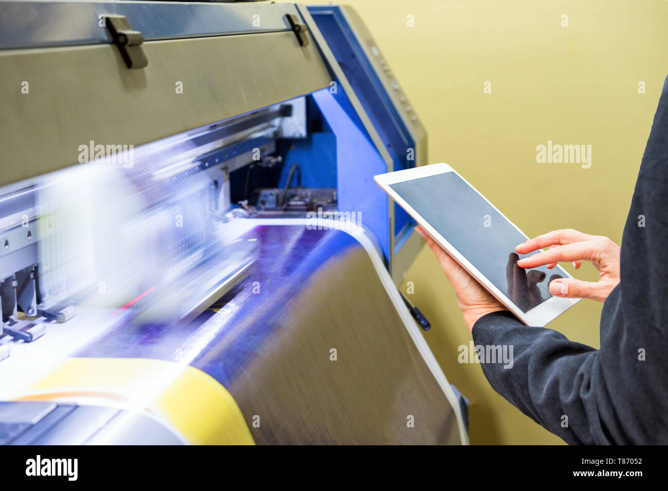 Technician using tablet control with format large inkjet printing blue ...
