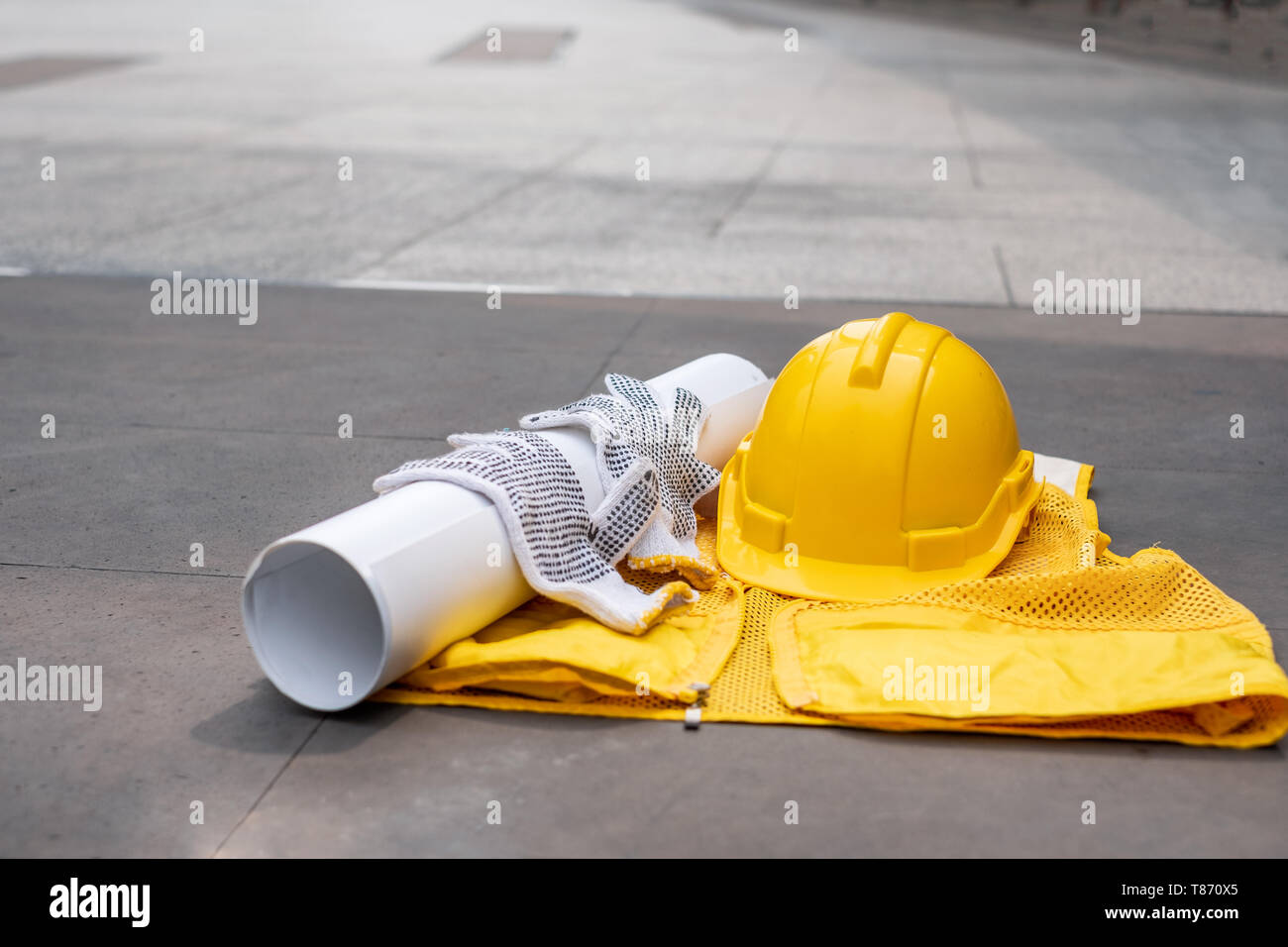 Yellow safety helmet with glove, blueprint on vest on concrete floor ...