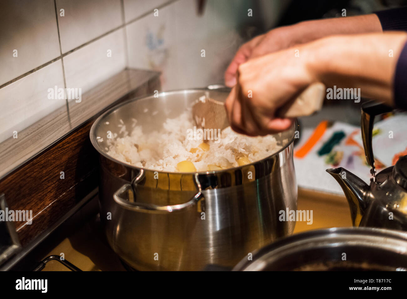 Hand chef using wooden flipper mixing rice with potato in stainless pot ...