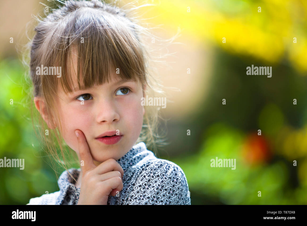 Portrait of cute pretty thoughtful child girl outdoors on blurred sunny ...